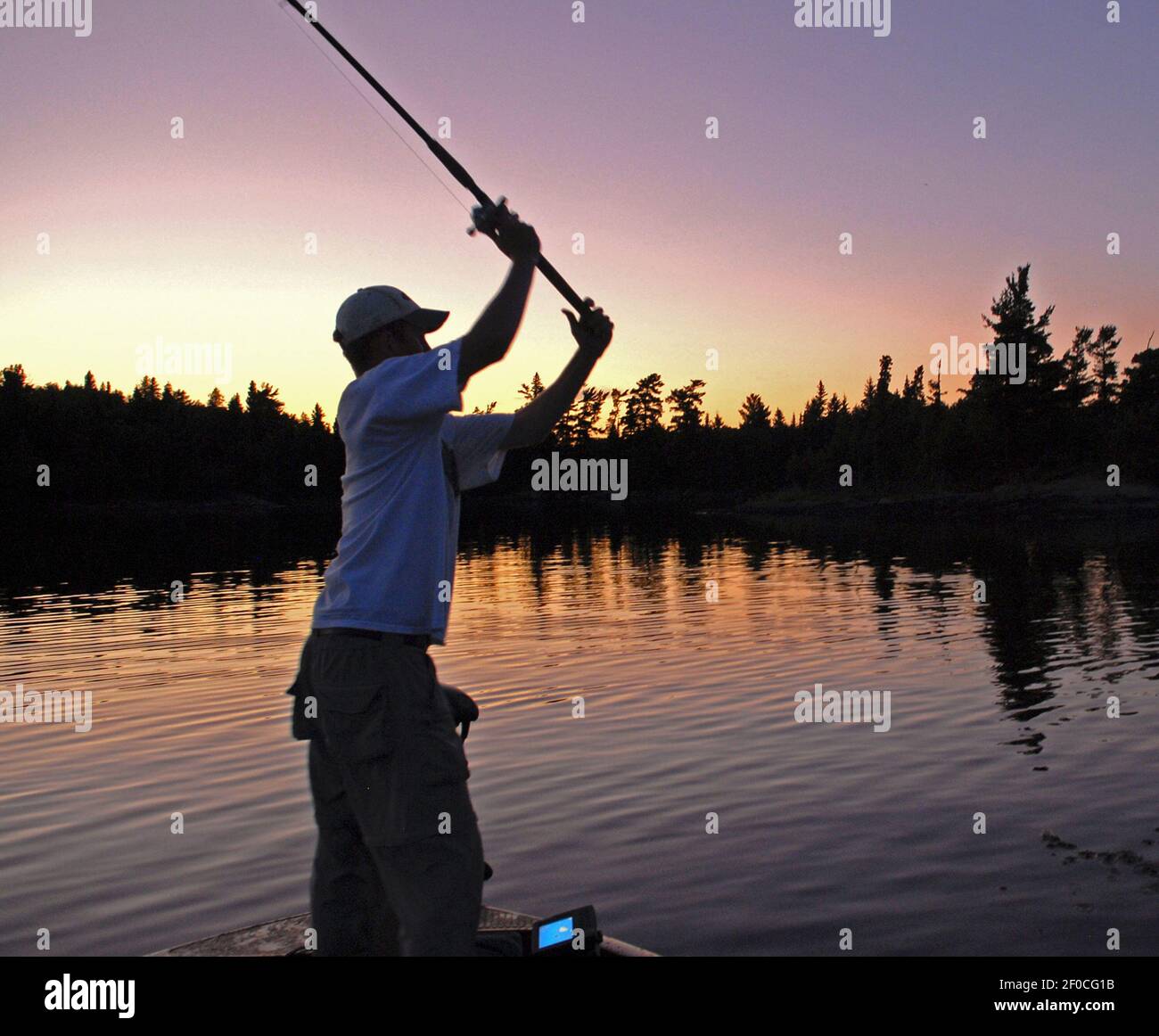 A muskie angler casts his line at sunset on Lake of the Woods in Canada ...