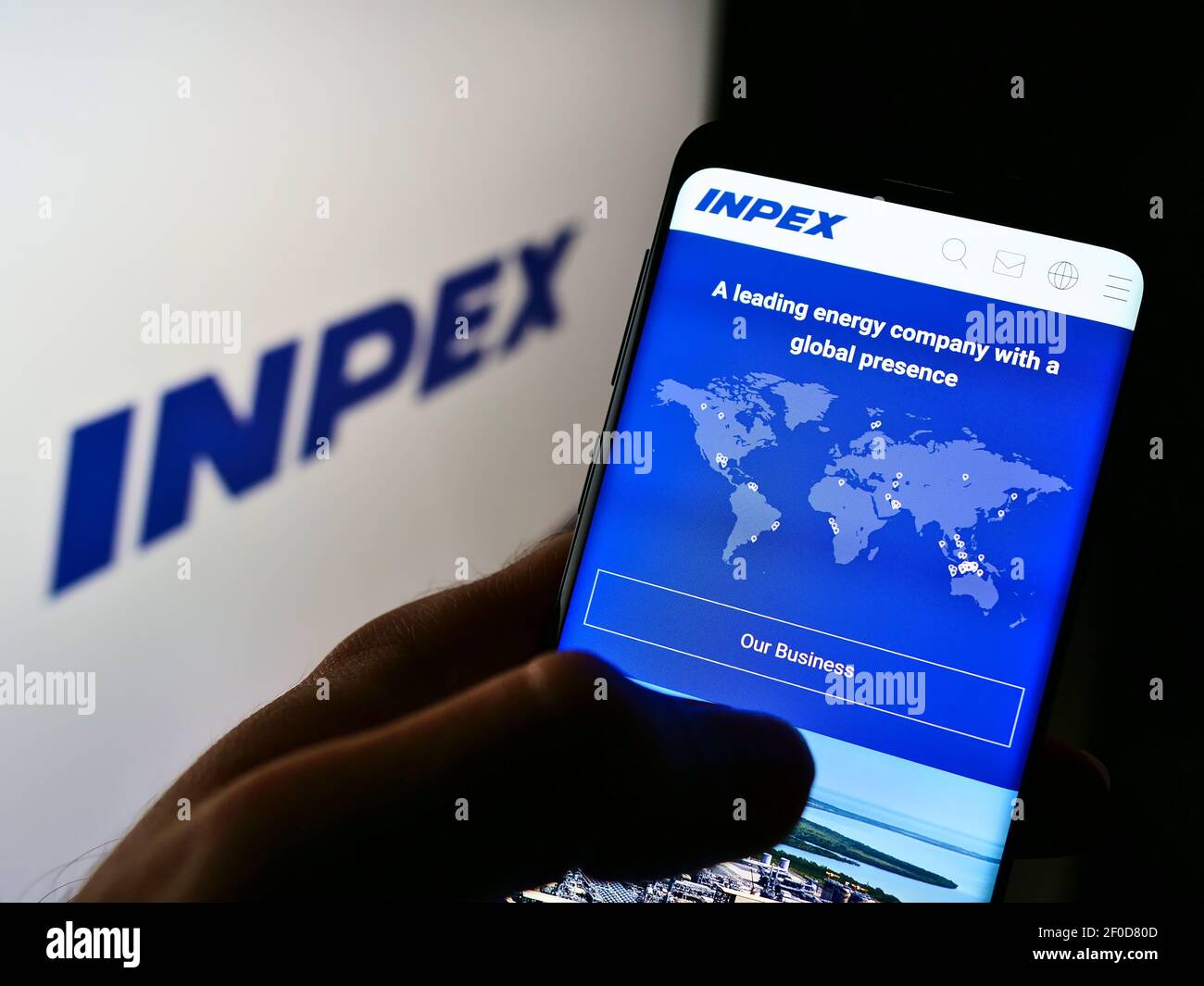Person holding mobile phone with web page of Japanese petroleum company Inpex Corporation on ...