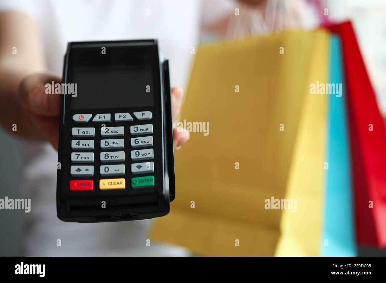 Mans hand holding pos terminal and many multicolored shopping bags ...