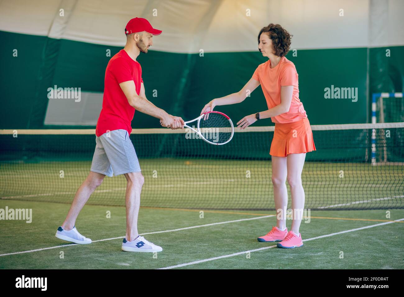 Man in a red cap and with a racket having a workout with his female ...