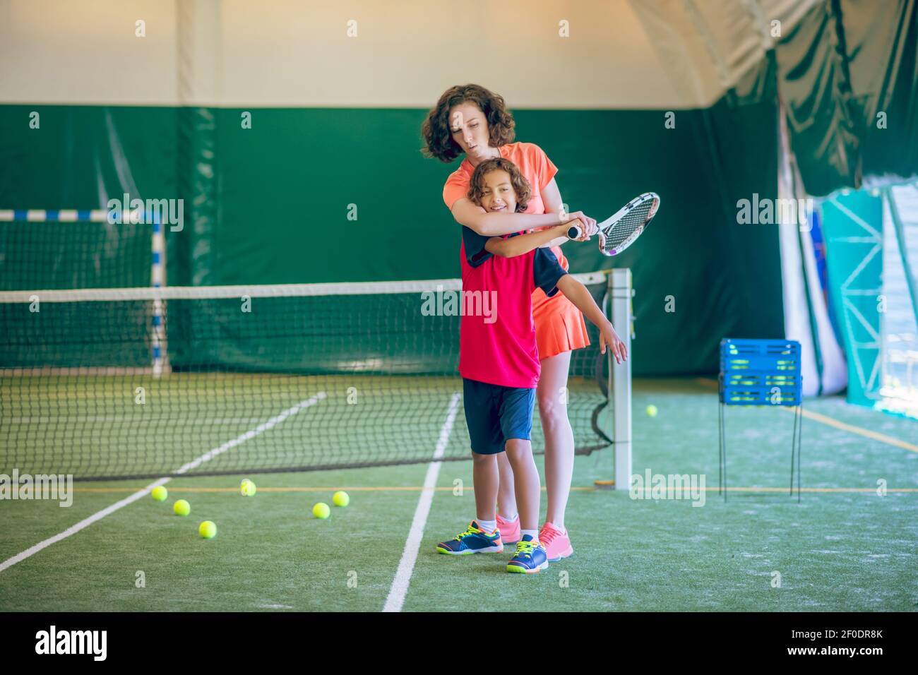 Woman in bright clothes teaching a boy to play tennis Stock Photo - Alamy