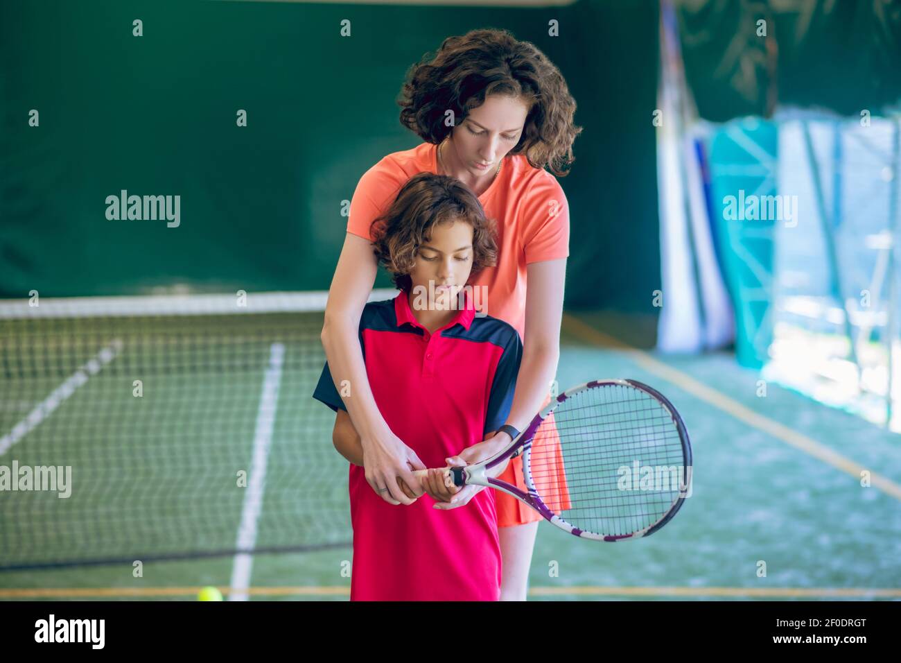 Female coach in bright clothes teaching a boy to hold a tennis racket ...
