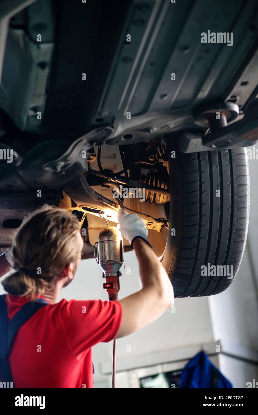 Man inspecting underside of raised car in garage Stock Photo - Alamy