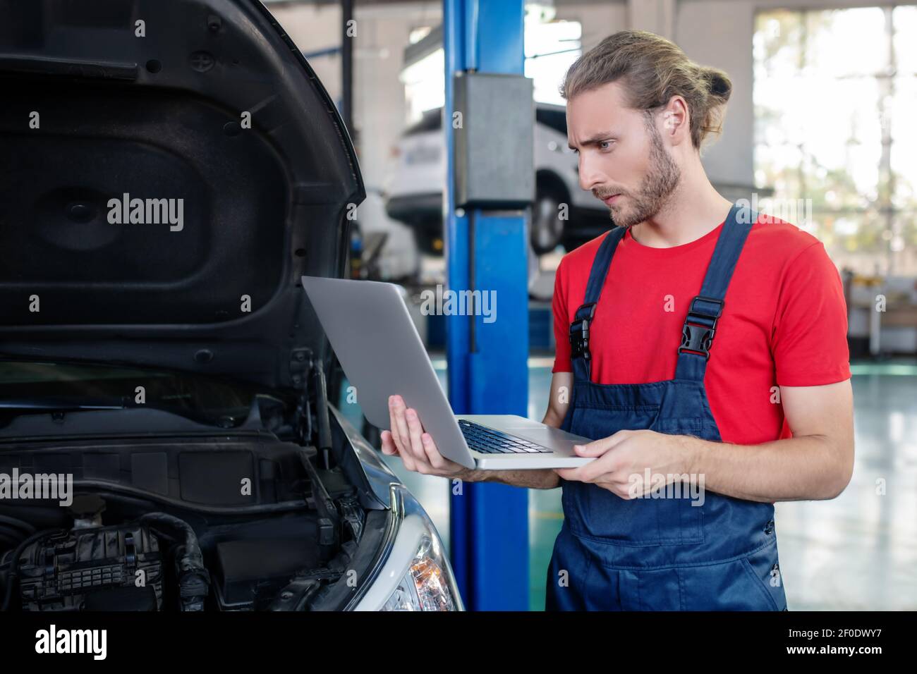 Serious man with computer near car in garage Stock Photo - Alamy