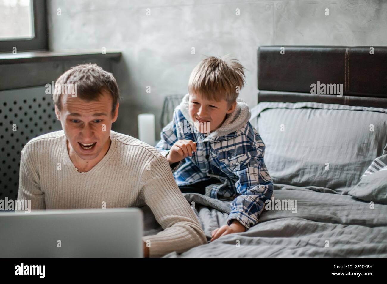 Dad and son at home sit by the bed and look at the laptop screen Stock ...