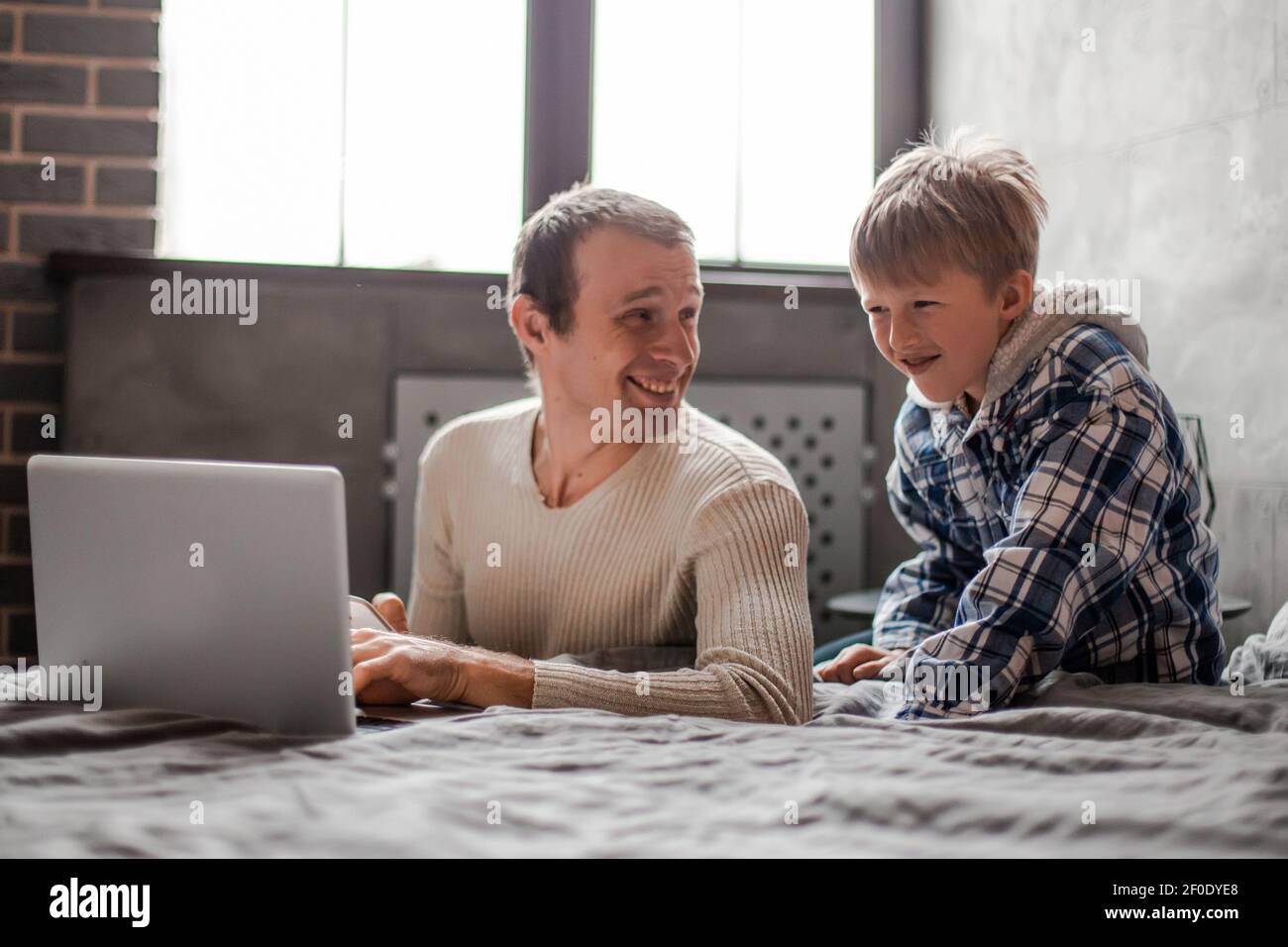 Dad and son at home sit by the bed and look at the laptop screen Stock ...