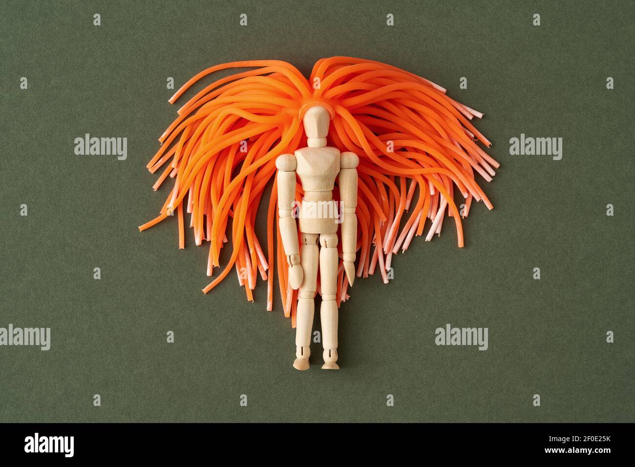 Wooden figure with orange plastic hair on green paper background Stock ...