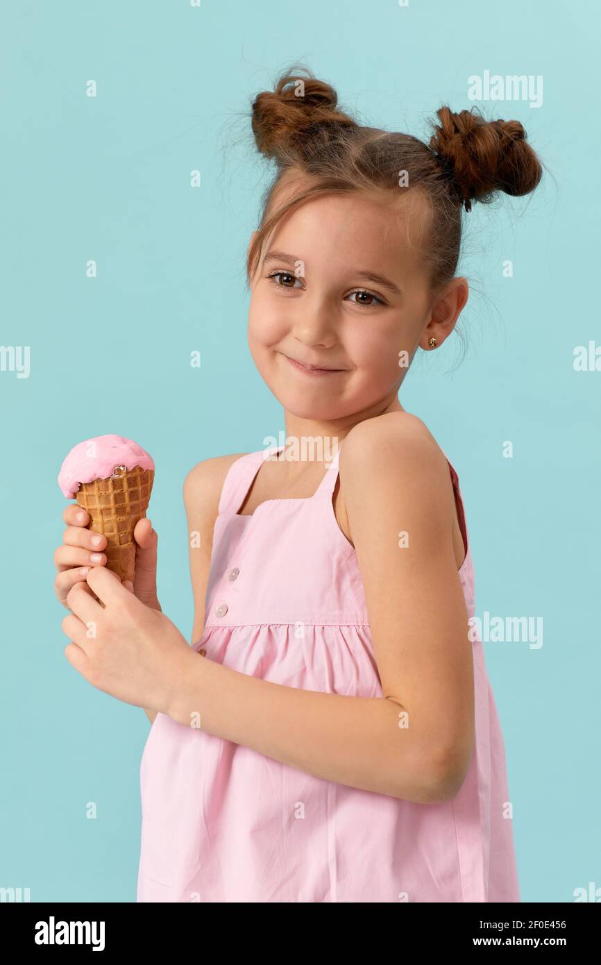 shy little girl eating strawberry ice cream in waffle cone on blue ...