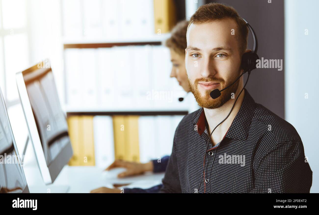 Red-bearded businessman talking by headset near his female colleague ...
