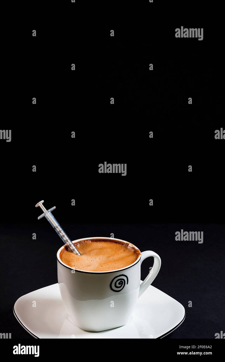 Coffee with milk on a plate with a syringe inside the coffee.This is a ...