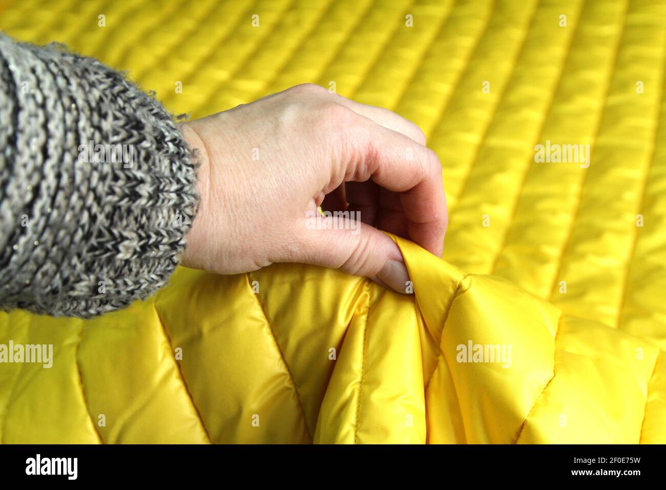 A woman's hand in a gray jacket holds a quilted yellow fabric Stock ...