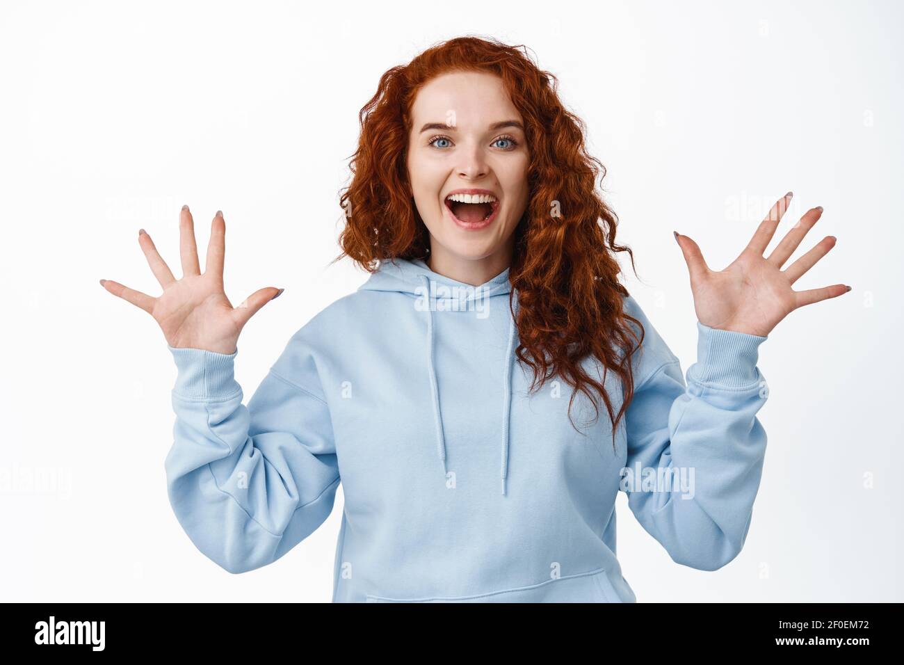 Portrait of cheerful ginger girl with curly hairstyle, raising hands up ...