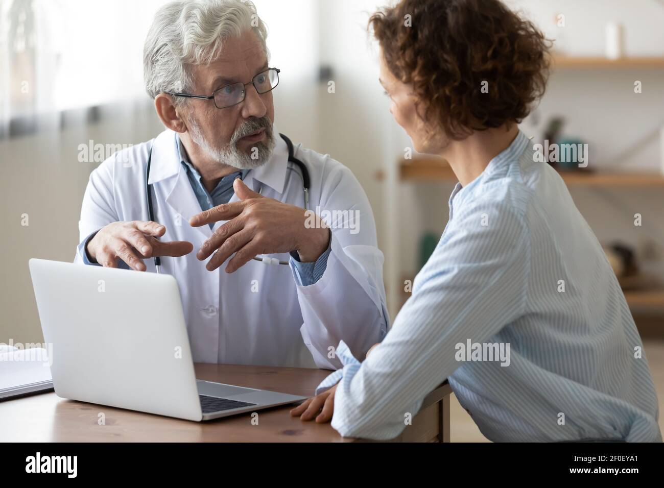 Senior doctor and patient discuss illness using laptop Stock Photo - Alamy