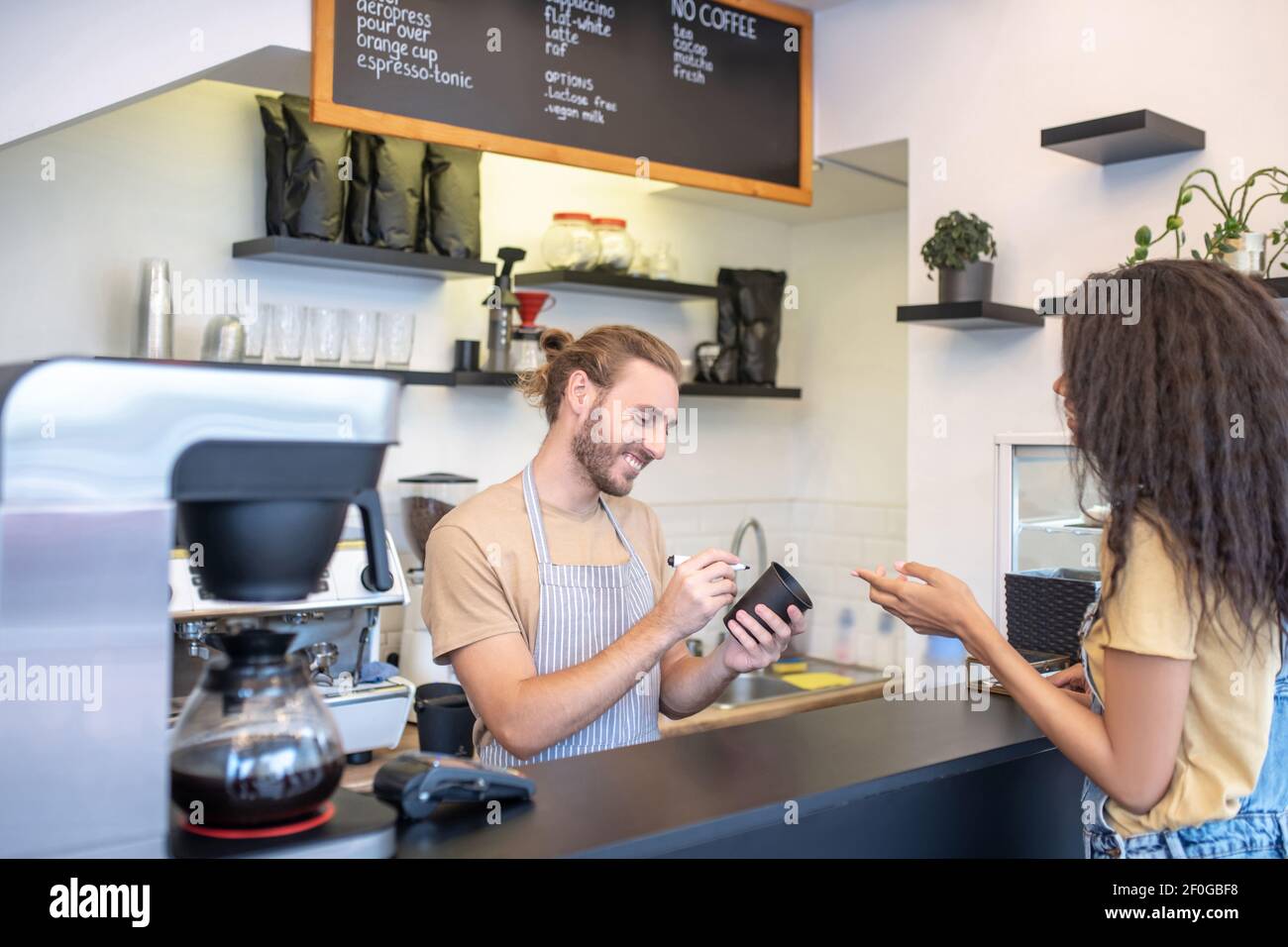 Man in apron at counter and woman making order Stock Photo - Alamy
