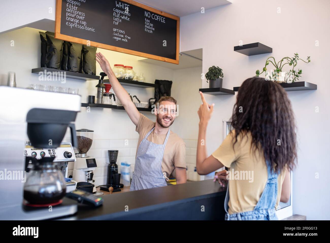 Man at counter offering choice of coffee and woman Stock Photo - Alamy