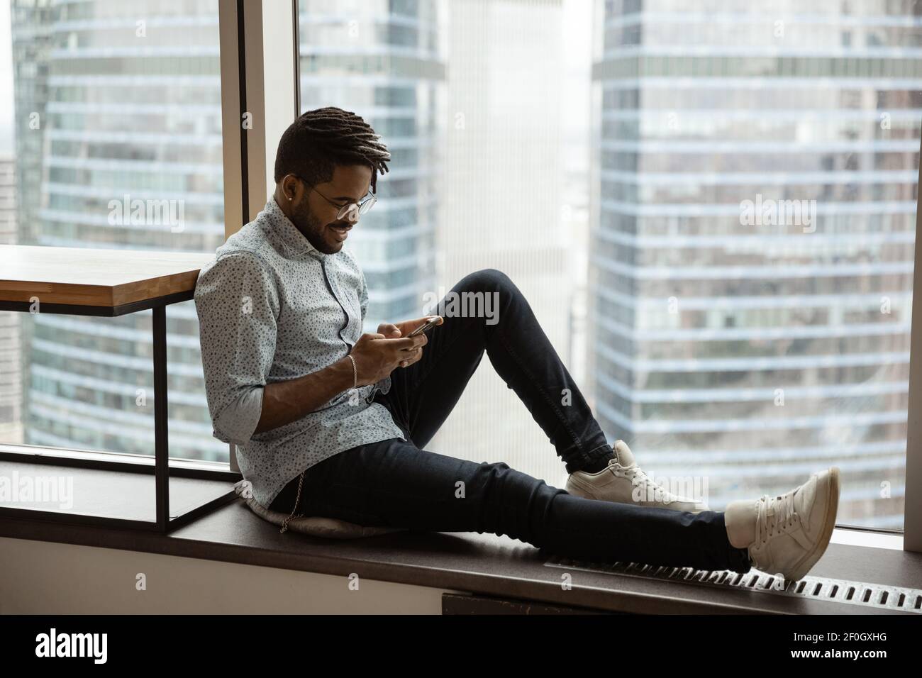 Side view smiling African American man using phone near window Stock ...