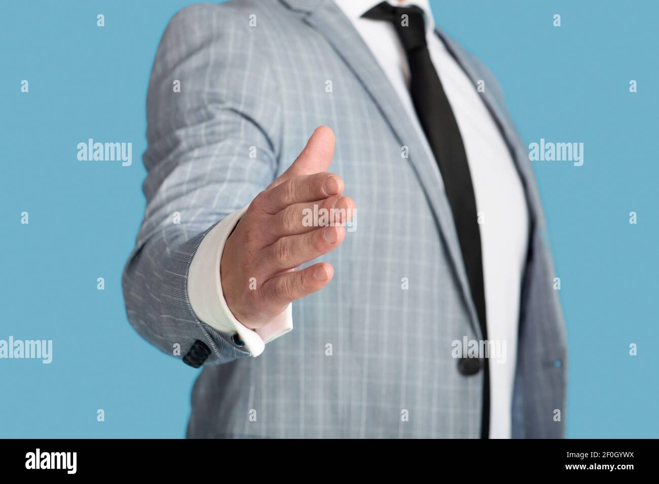 Untrecognizable young businessman offering hand for handshake on blue ...