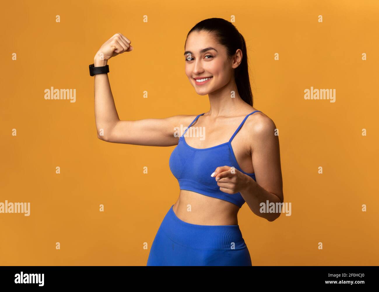 Sporty woman showing biceps and pointing to camera Stock Photo - Alamy