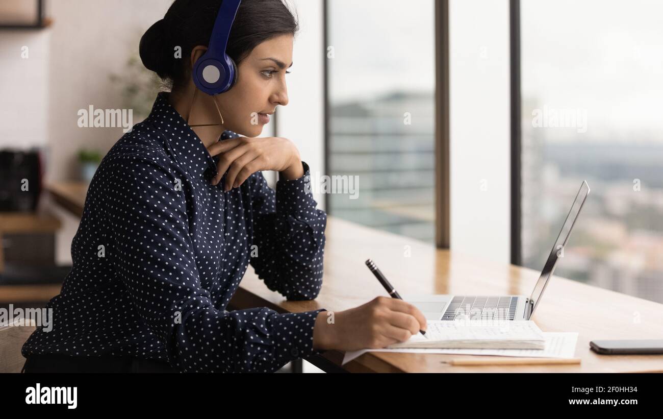 Close up focused Indian woman wearing headphones taking notes Stock ...