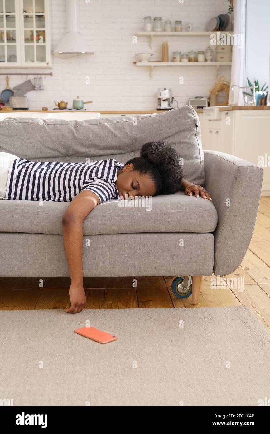 Exhausted African American woman sleeping on couch at home, dropping ...