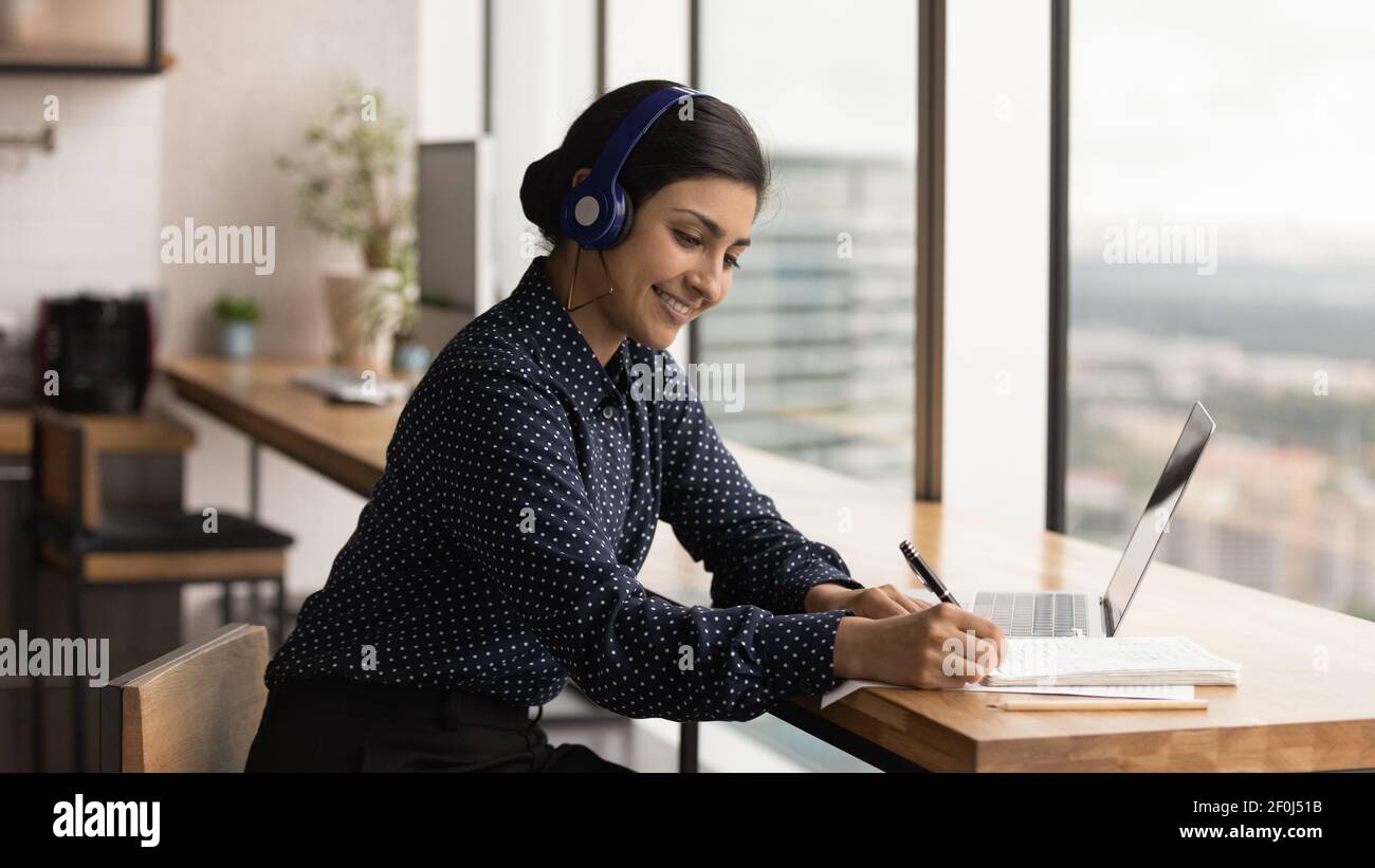 Close up smiling African American woman wearing headphones taking notes ...