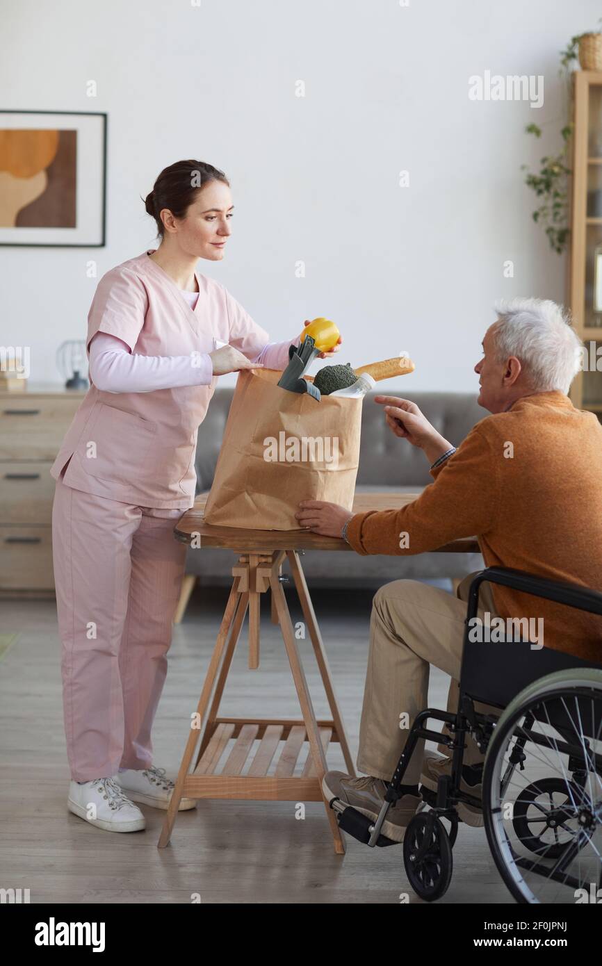 Vertical full length portrait of young female caregiver bringing ...