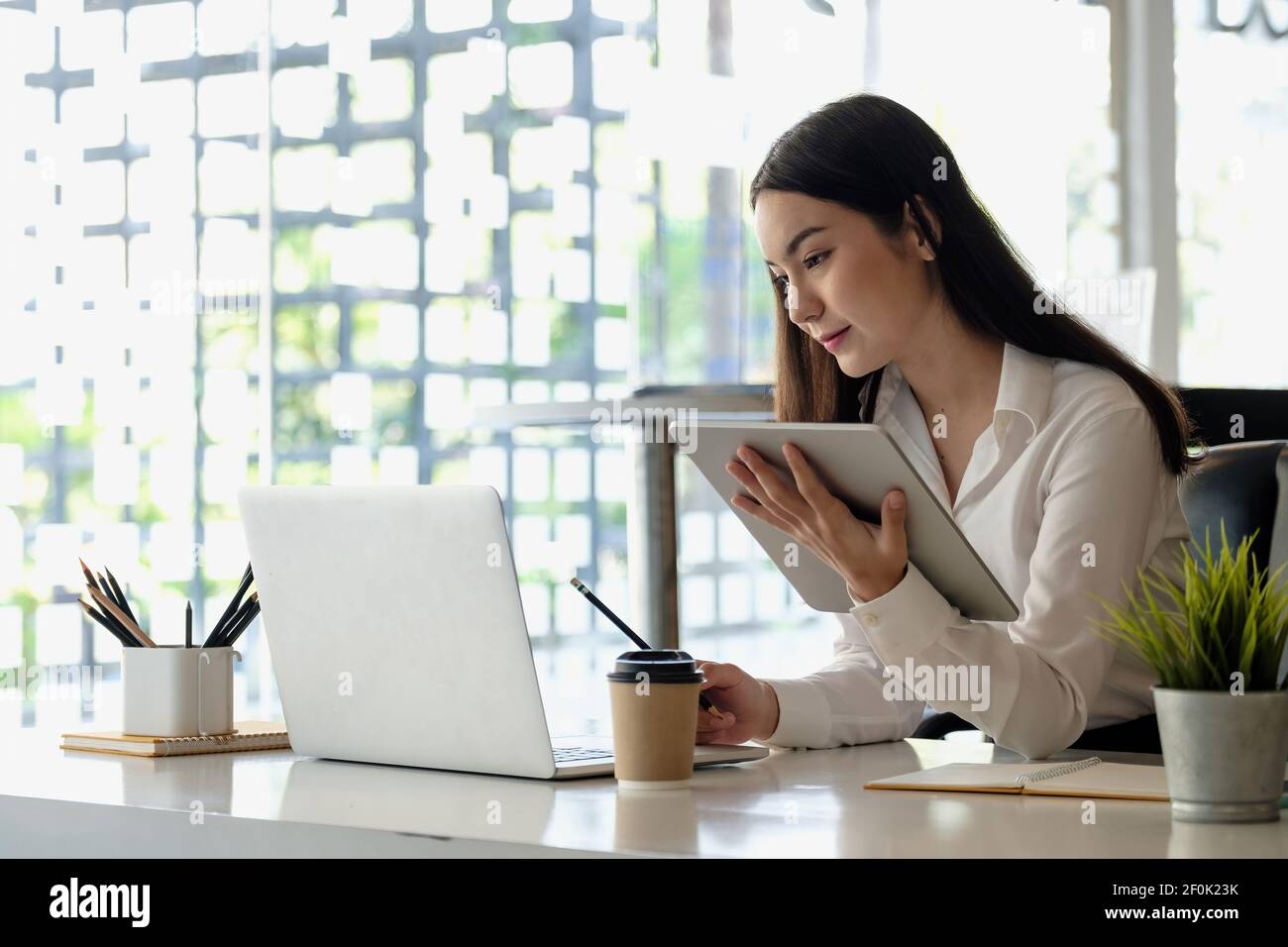 Beautiful business woman uses tablet and laptop while working in the ...