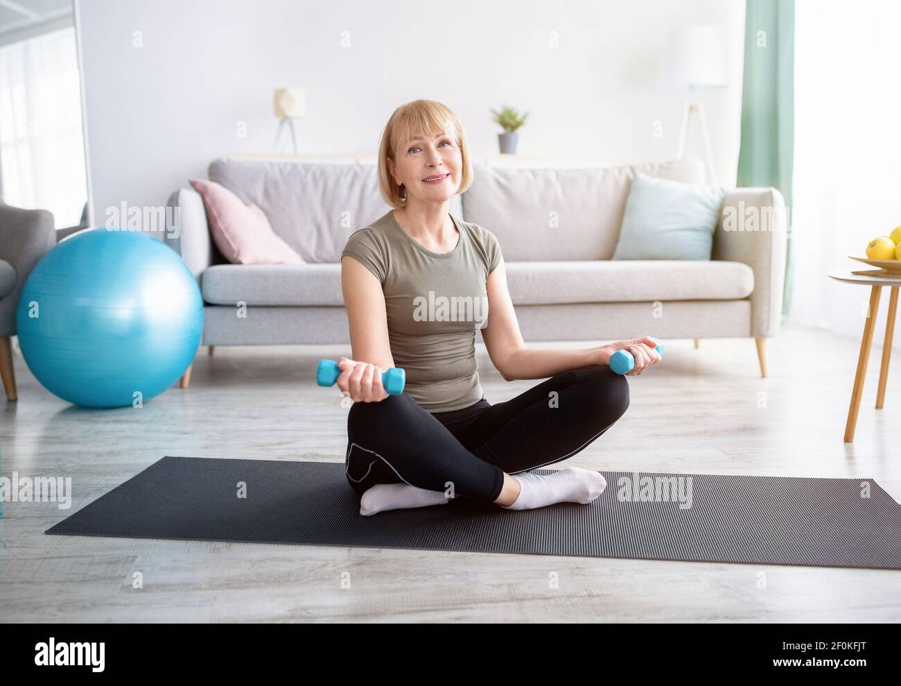 Positive mature woman in sports clothes doing strength exercises with ...