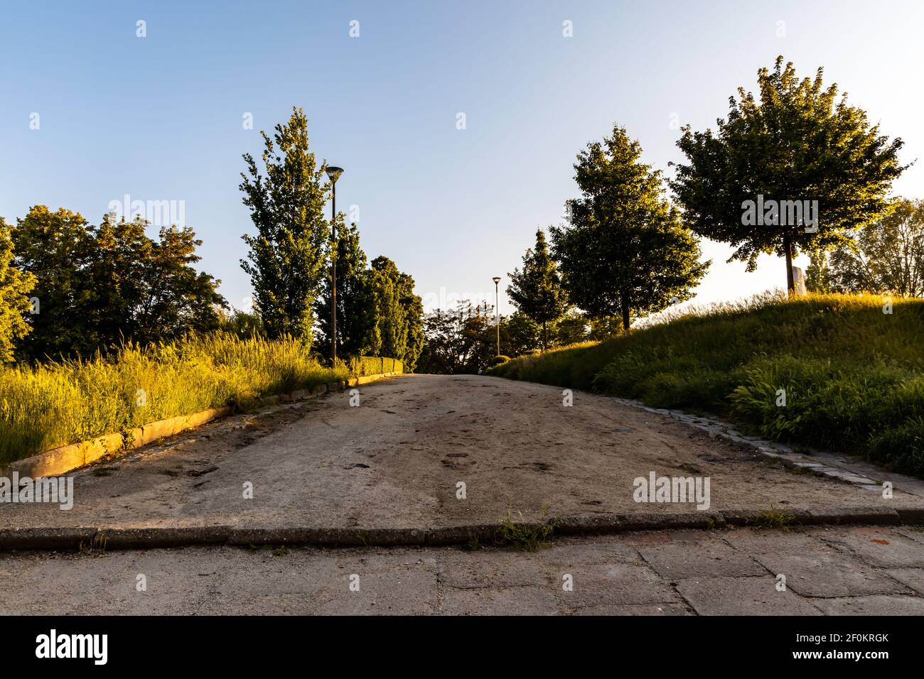 Wide path at small hill with park on top at sunset Stock Photo - Alamy