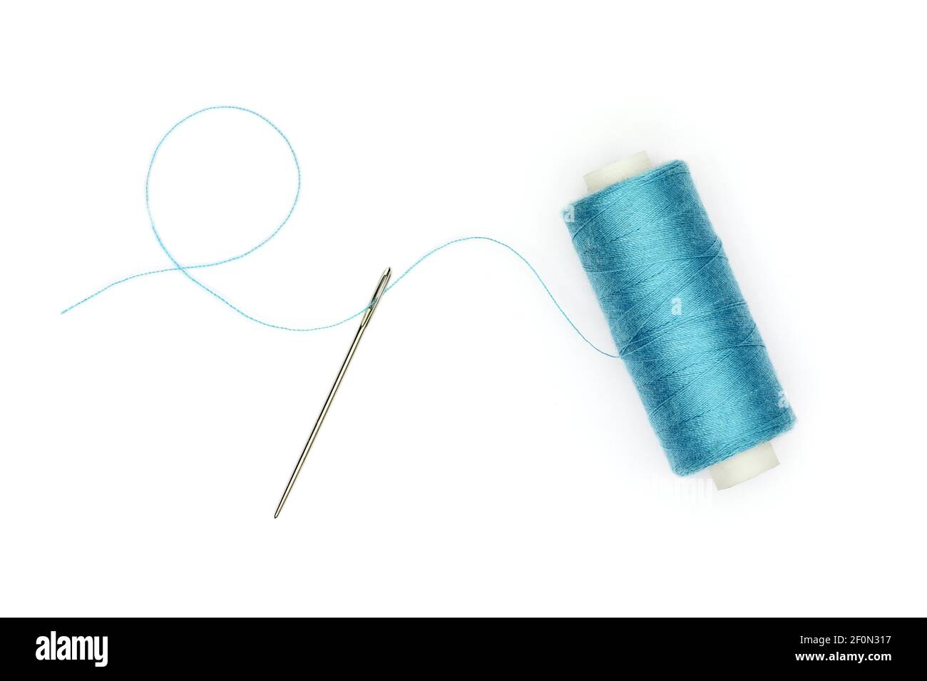Sewing concept: Spool of blue thread with thread passing through the ...