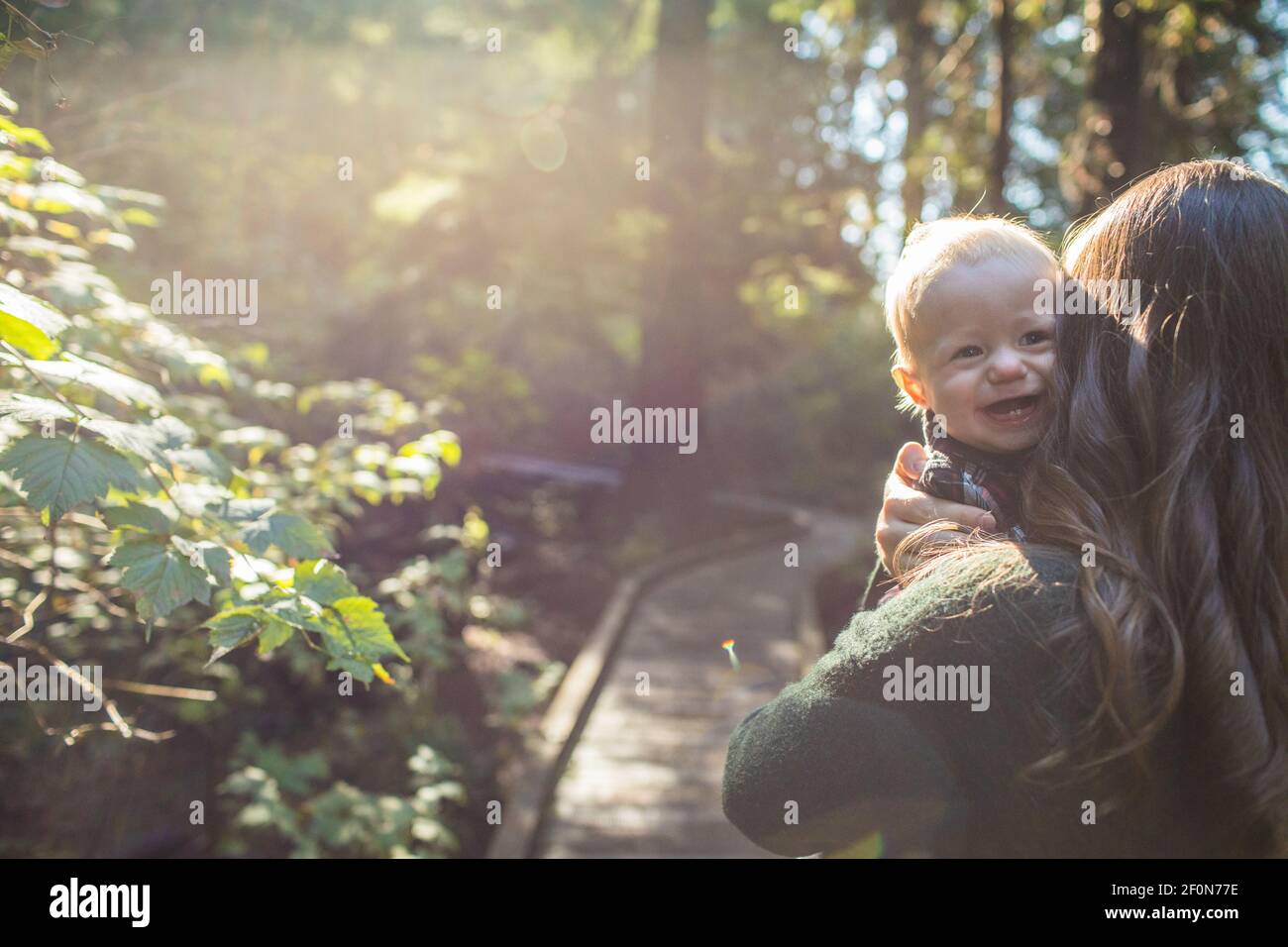 Smiling young boy looking over mothers shoulder Stock Photo - Alamy