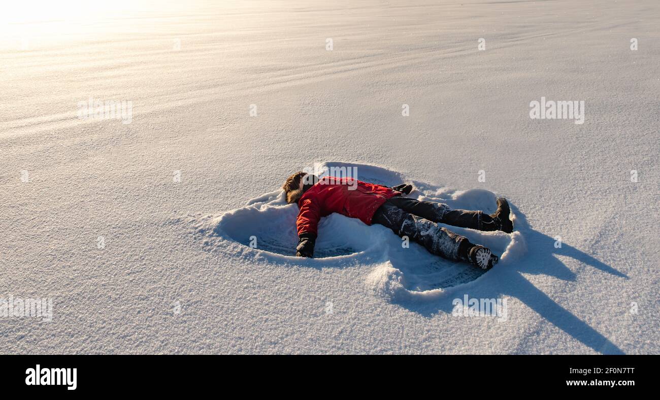 Child making a snow angel in an open snowy field in the morning sun ...