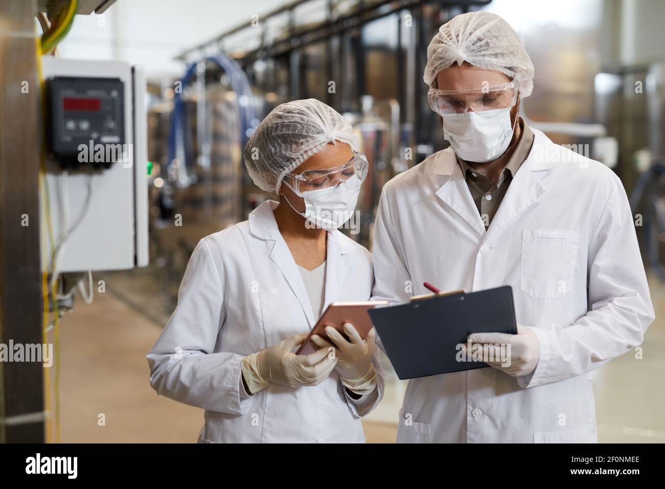 Waist up portrait of two workers wearing masks and lab coats while ...