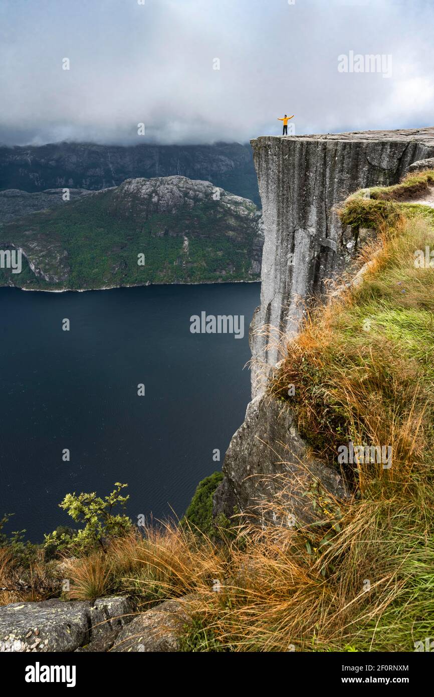 Person standing on steep cliff, Preikestolen rock spire, Lysefjord ...