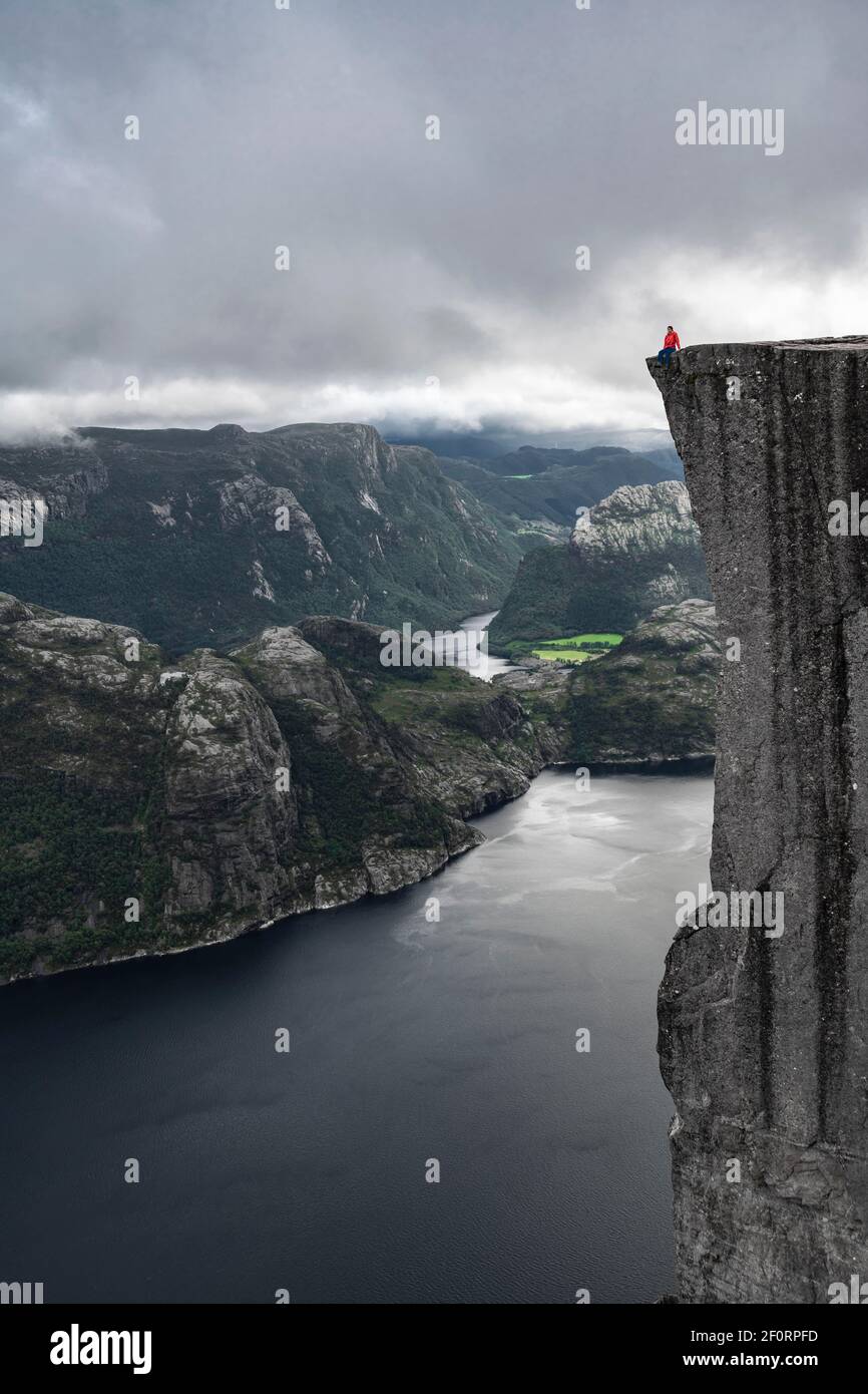 Person sitting on steep cliff, Preikestolen rock spire, Lysefjord ...