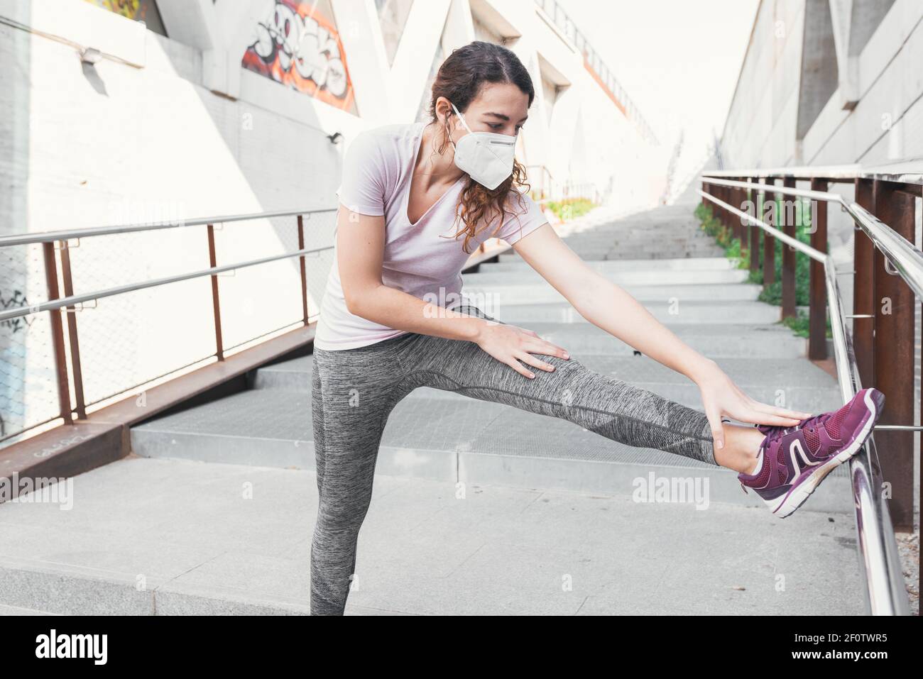 Woman with face mask dressed in sportswear stretching one leg on a ...