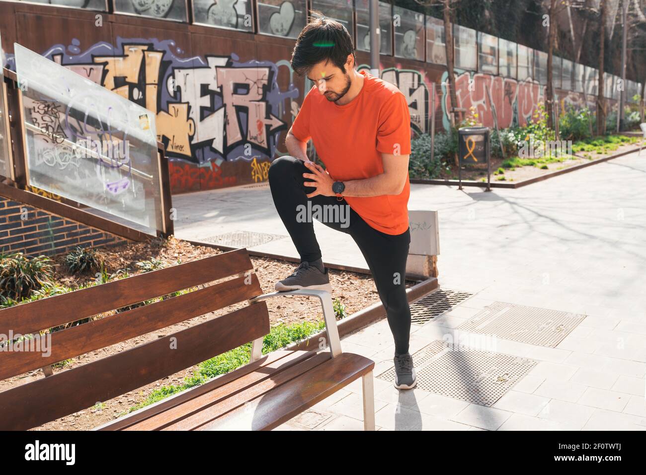 Man in sportswear bending his leg on a bench in the street Stock Photo ...