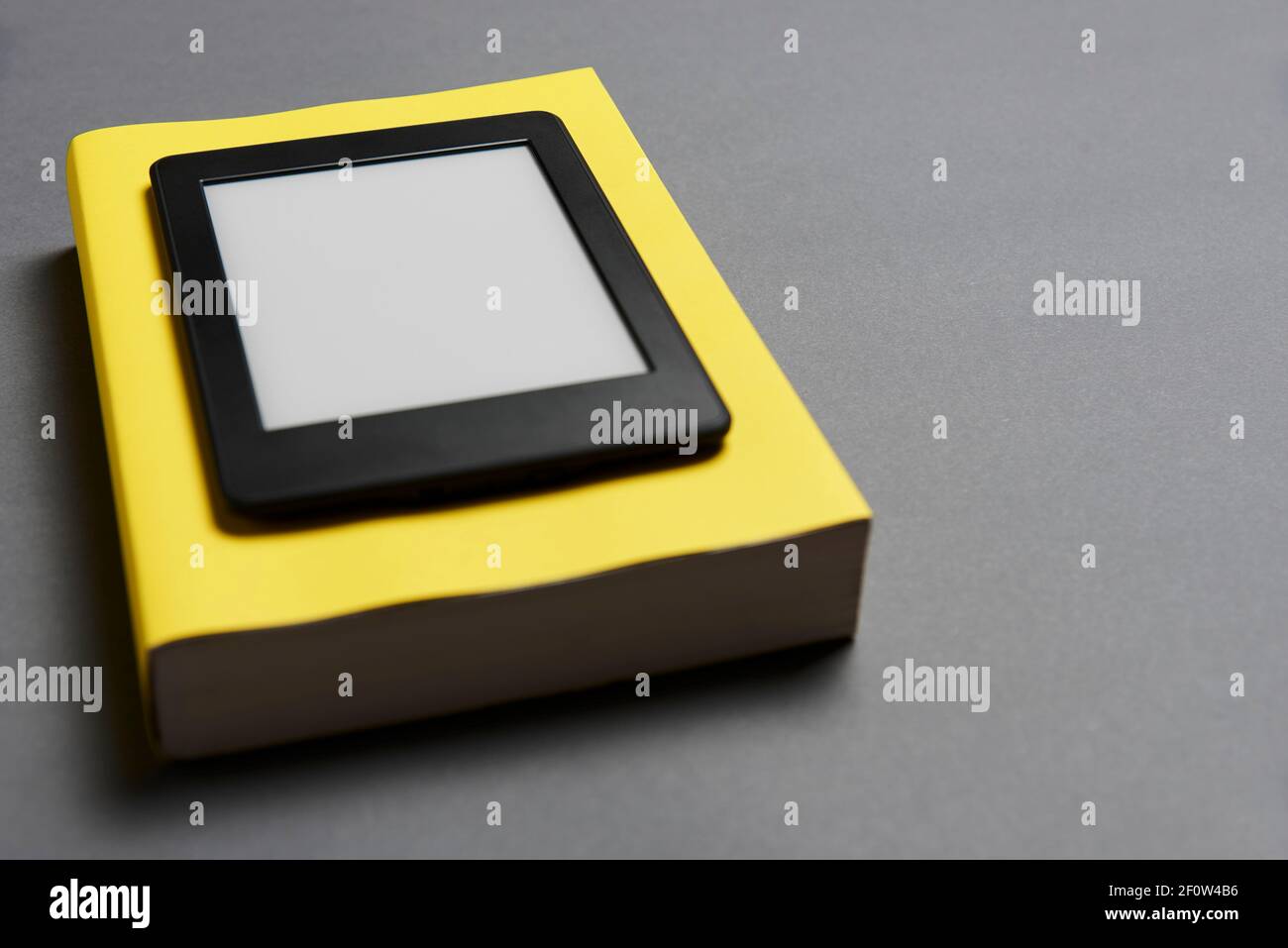 Electronic reader with blank screen and closed yellow book on gray ...