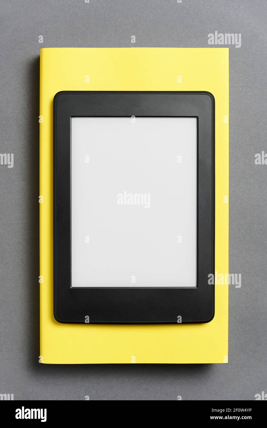 Electronic reader with with blank screen over a closed yellow book on a ...