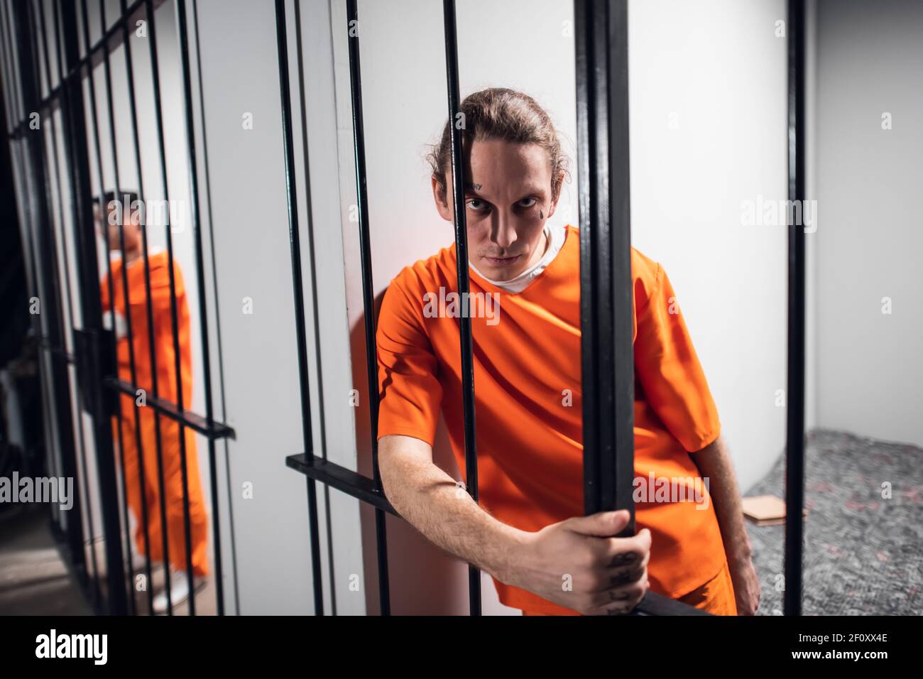 Harsh wild prisoner criminal maniac with tattoos grabs the bars. A ...