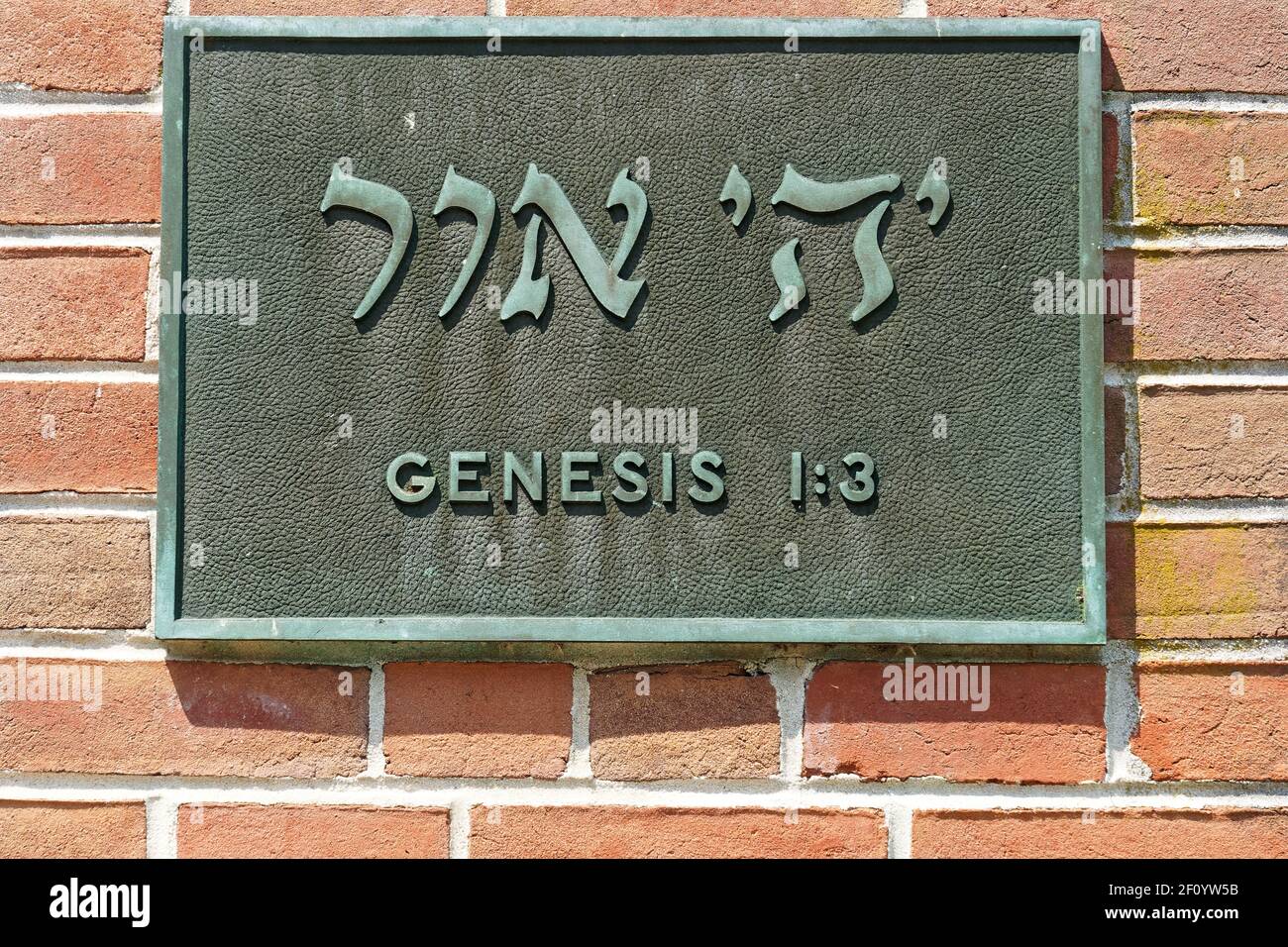 textured bronze plaque hanging on a red brick wall with the Hebrew text ...