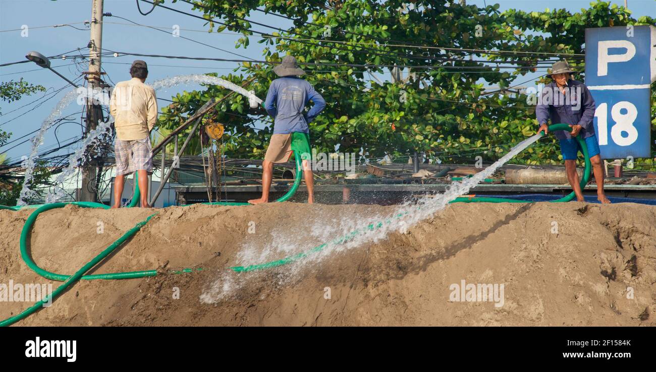 Workers at an aggregate company hosing down a pile of building sand ...