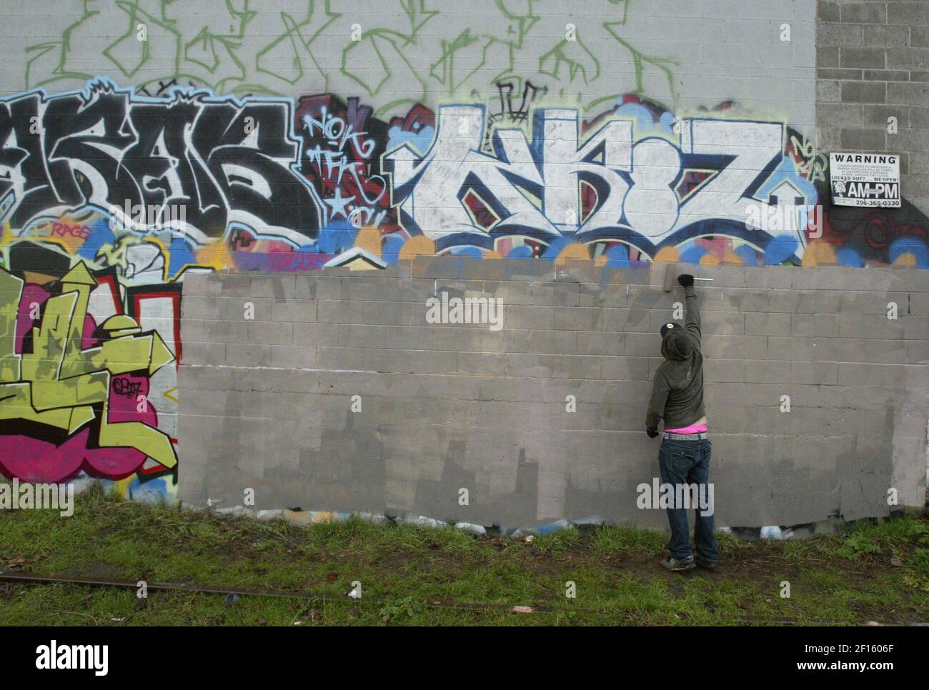 A "writer" covers over other graffiti, preparing his "canvas" on a SoDo ...