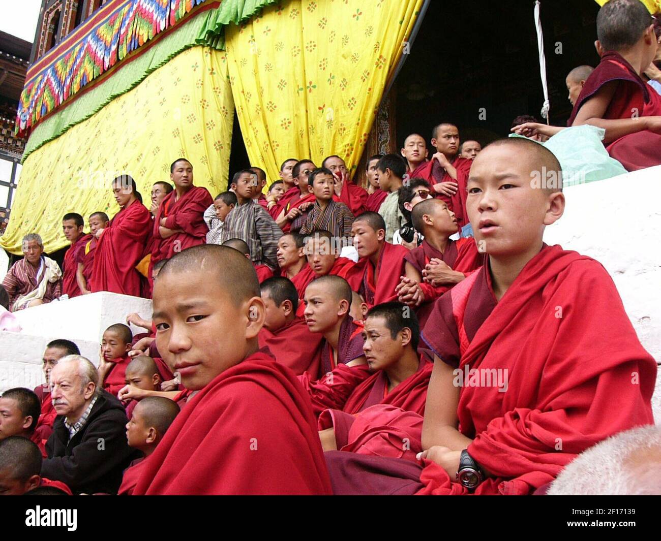 Hundreds of Buddhist monks in crimson robes watch the masked dancers ...