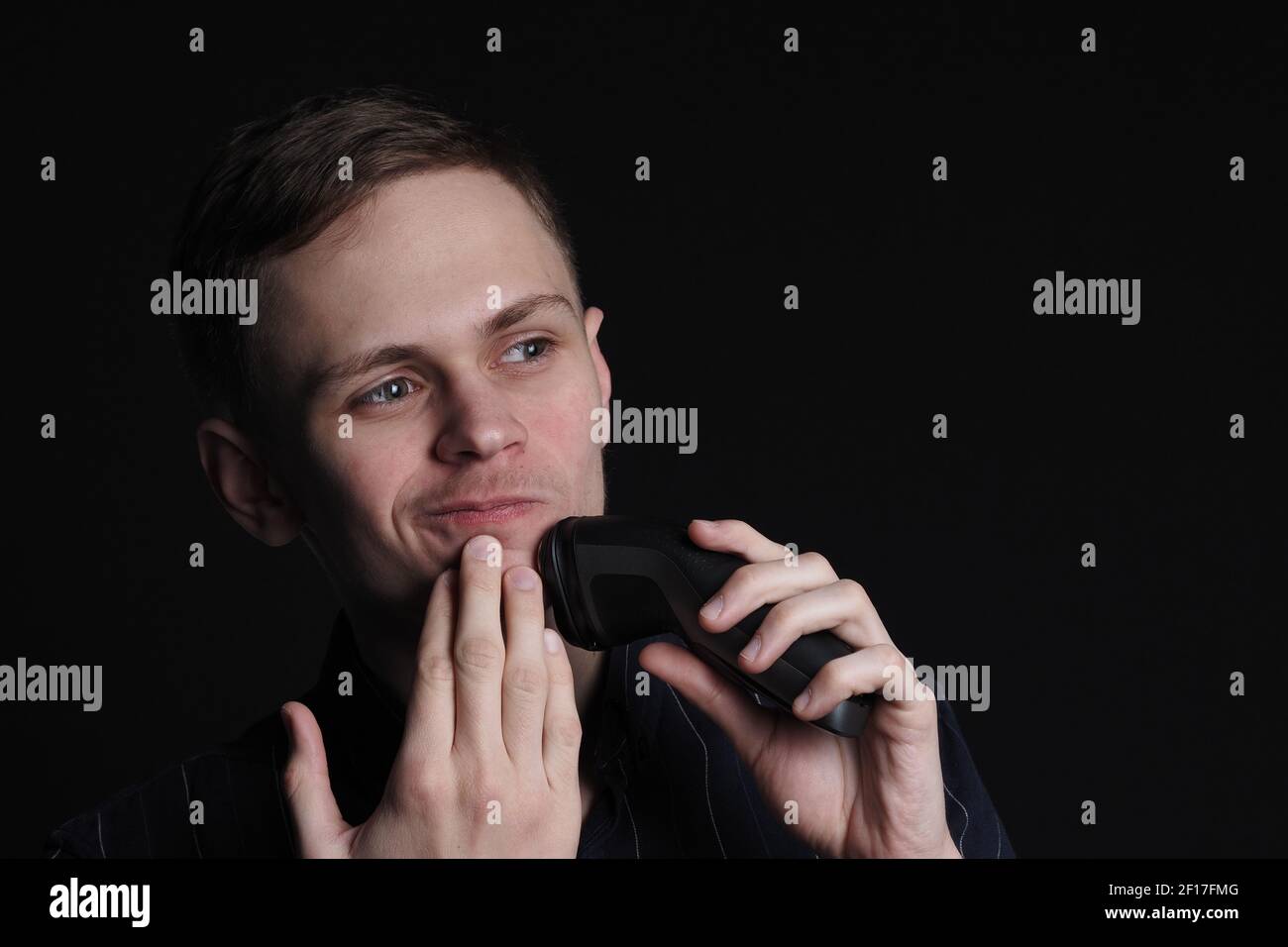 A young man shaves his face with an electric razor Stock Photo - Alamy