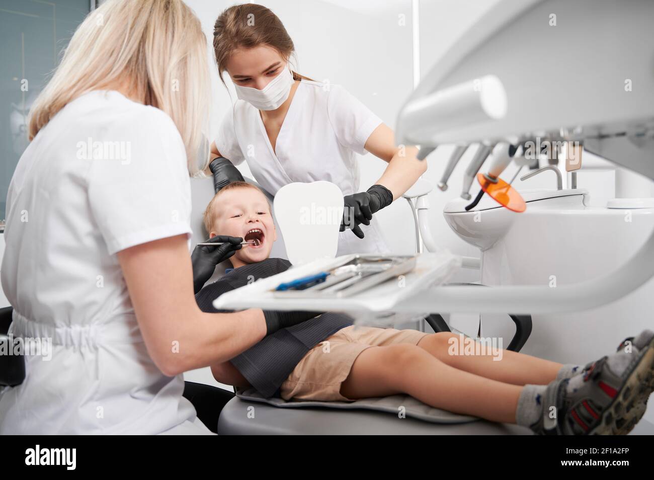 Little boy sitting in dental chair while two female dentists checking ...