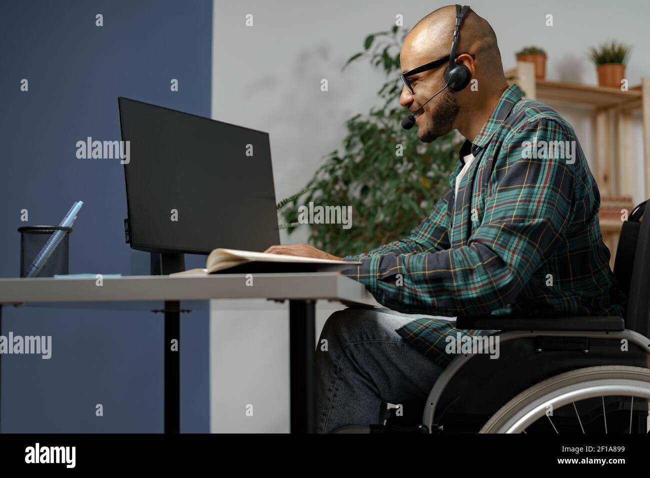 Disabled young man in wheelchair working at his working table with ...