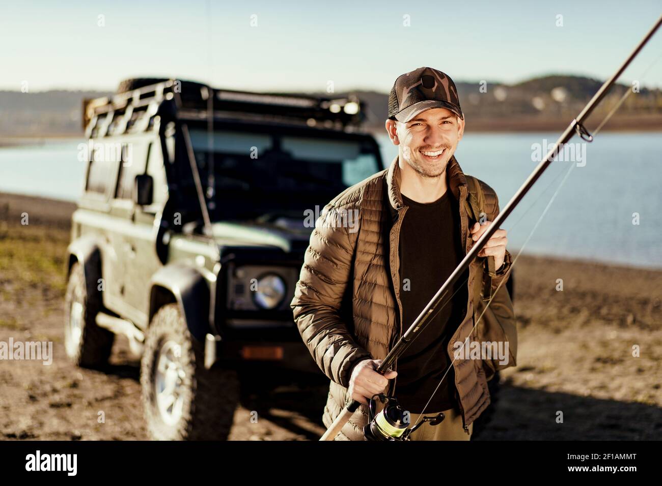 Young fisherman standing near his car and holding fishing equipment ...