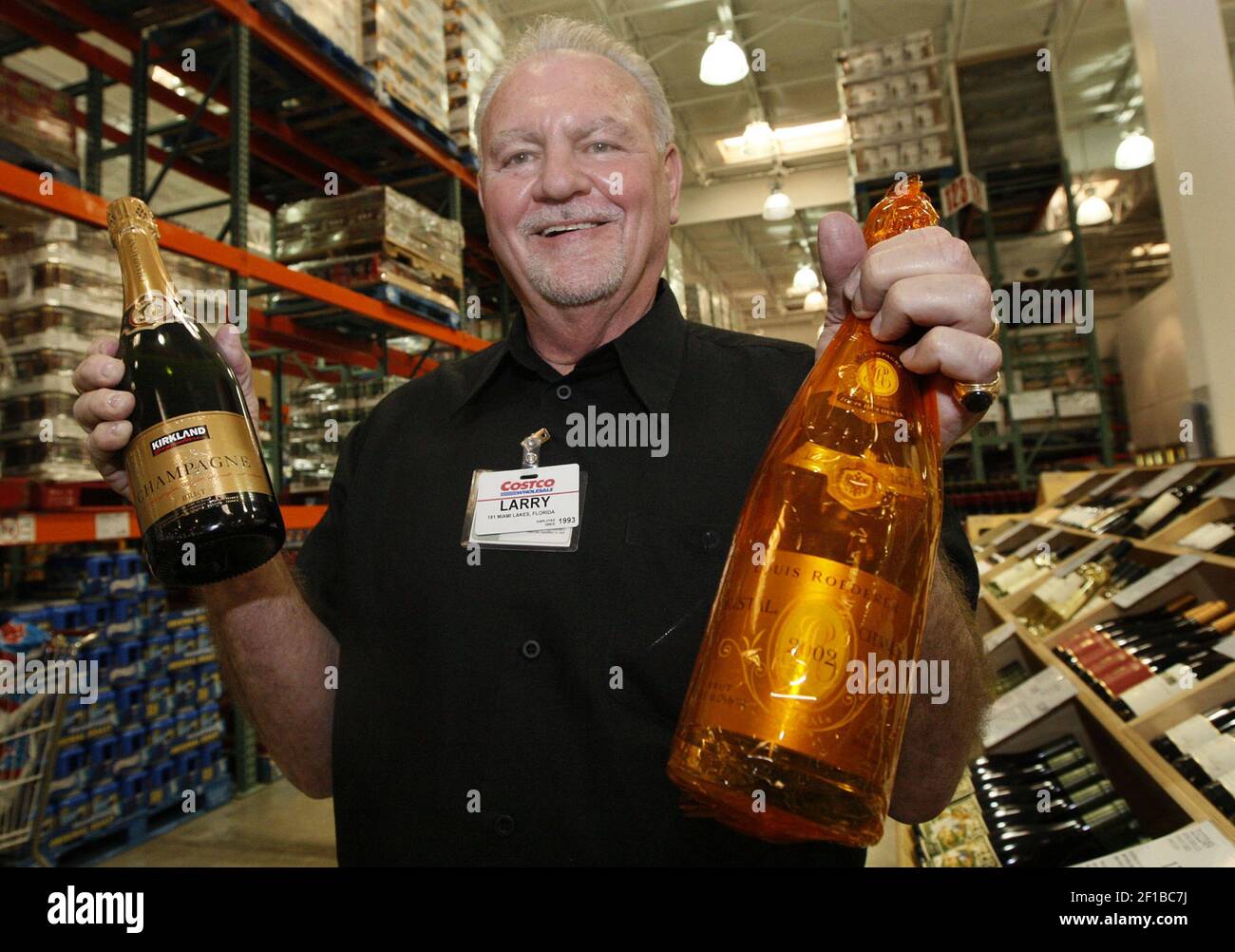 Costco manager Larry Lewis holds two bottles of champagne, one high end ...
