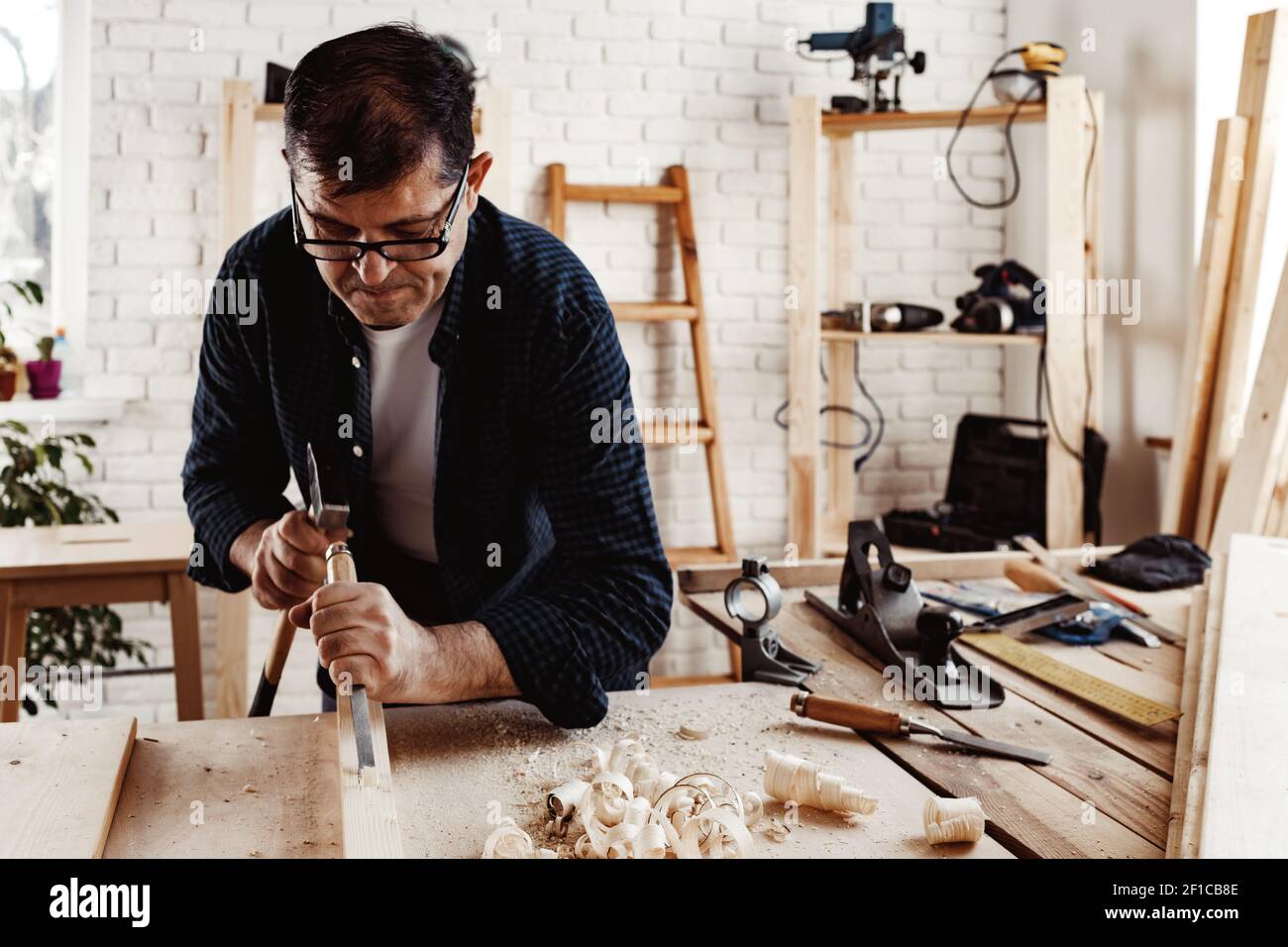 Middle-aged man carpenter working in a workshop with chisel and hammer ...